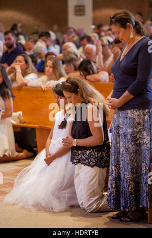 A Hispanic mother and daughter pray during First Communion mass at a ...