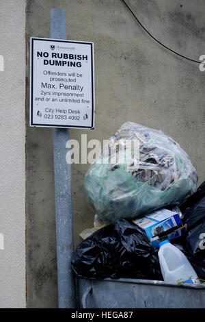 a garbage filled skip next to a sign saying no rubbish dumping england ...