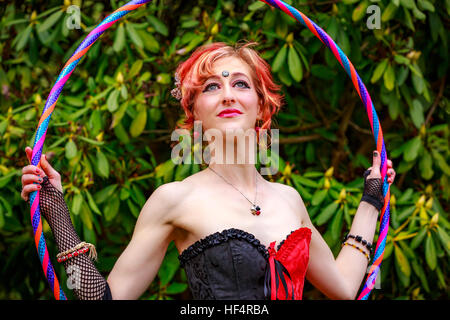 Young beautiful woman in circus costume play with hula hoop in the park ...