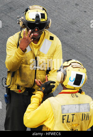 A flight deck crewman uses hand signals to communicate with other ...