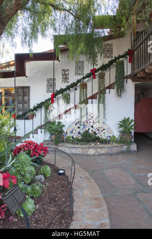 Plaza center with hanging plants and pots on stairs against an adobe ...