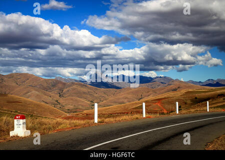 Empty road winding among rocks and lush green hills with pine trees ...