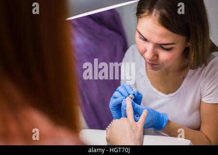 Manicurist is applying electric nail file drill to manicure on female ...