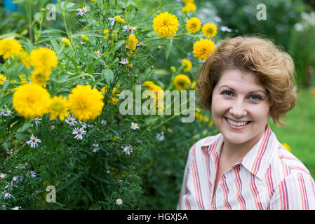 smiling curly woman in yellow knitted sweater showing heart sign on ...