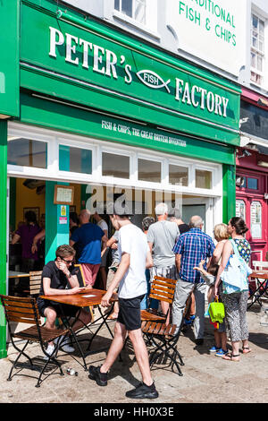 Long mid-day queue of people for fish and chip shop on seafront during ...