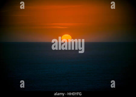 A red burning sunset over the sea with rocky volcanic cliff. Abstract nature summer ocean sea ...