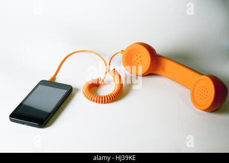 Orange analog phone and smartphone connected by a cable Stock Photo - Alamy