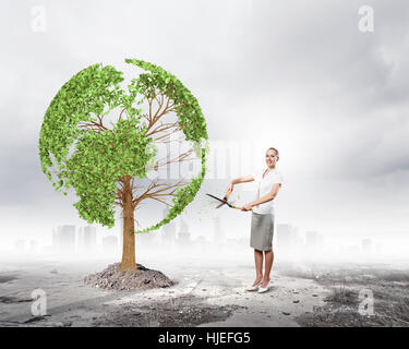 Young businesswoman cutting tree with scissors in shape of Earth planet ...