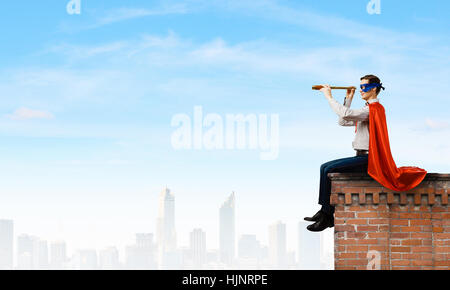 Superman in cape and mask sitting on top of building Stock Photo - Alamy