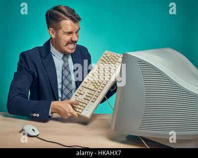 Angry businessman breaking keyboard against blue background Stock Photo ...