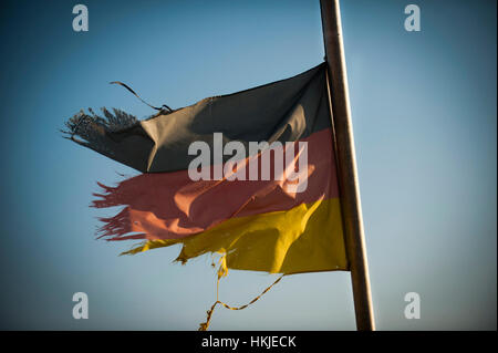 German national flag torn in the wind ists waving in front of blue ...