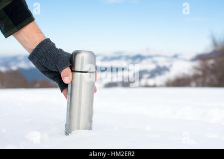Thermos with coffee in hand. Landscape with snow-covered ridge of Altai ...