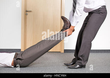 Businessmen pulling colleague's leg at office Stock Photo - Alamy