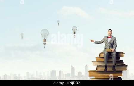 Young businessman sitting on pile of giant books Stock Photo - Alamy