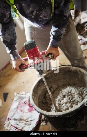 Male builder mixing plaster in bucket using electric mixer closeup ...
