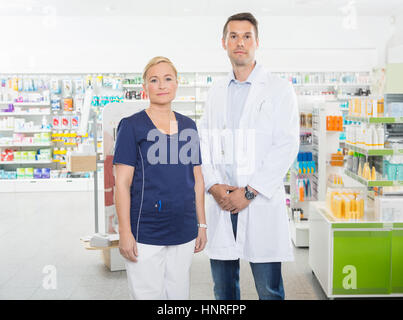 Pharmacist with female assistant in pharmacy standing in front of shelf ...