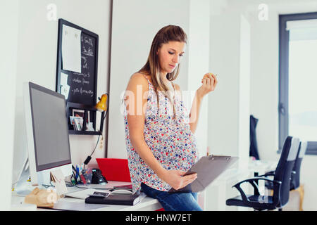 Young pregnant woman holding clipboard afraid and shocked with surprise ...