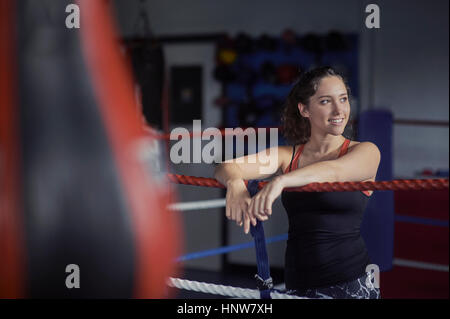 Female boxer leaning on ropes and looking at camera in boxing ring at ...