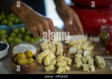 Close-up of staff arranging piece of cheese on wooden board in grocery ...