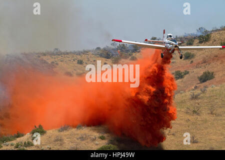 Plane dropping fire retardant on a bush forest wildfire on hills next ...