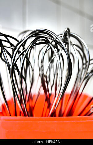 Metal food whisks in red plastic container against white tiled kitchen ...