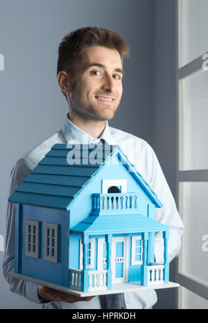 Friendly real estate agent with light blue model house Stock Photo - Alamy
