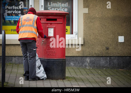 Postman in uniform emptying letters from a red Royal Mail postbox at ...