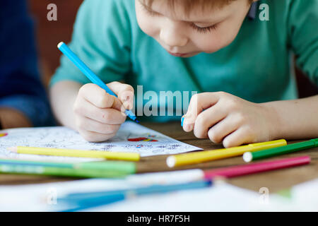 Teacher of drawing bending over boy sitting by table among other little ...