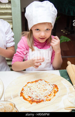 Adorable little girl in chef's coat and cap cooks at the children's toy ...