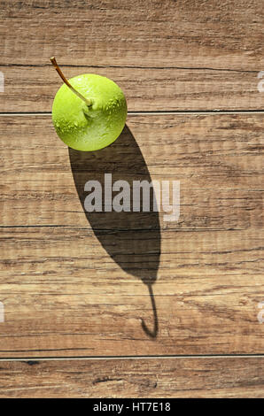 Alone juicy green pear with water drops cast a long shadow on wood ...