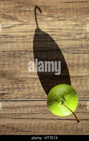 Alone juicy green pear with water drops cast a long shadow on wood ...