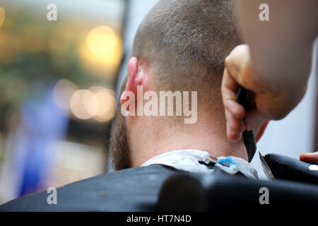 Hairdresser coiffeur makes hairstyle with electric trimmer and comb ...