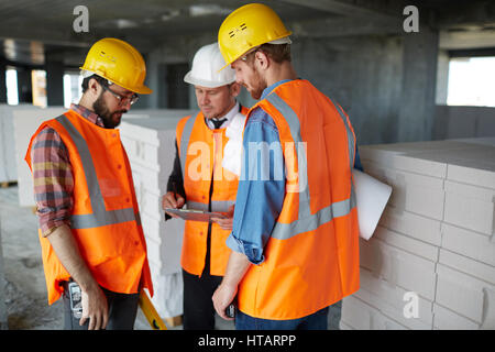 Group of three workmen wearing protective helmets and vests standing ...