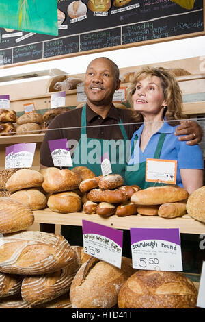Two smiling bakers, a woman and man, holding an open sign in a cozy ...