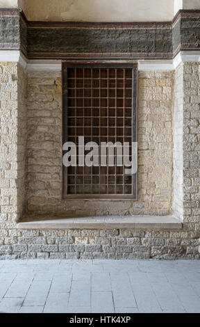 Recessed wooden window with decorated iron grid over stone bricks wall ...