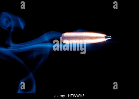 Copper plated bullet on a black background with white smoke trailing ...