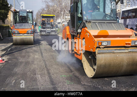 Asphalt paver and road roller machines on a construction site in a park ...