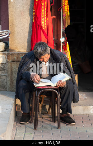 A man reads a book while sitting in the sun along the Seine River in ...