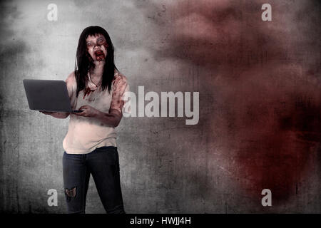 Female zombie holding laptop over burn city background. Halloween ...