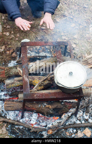 metal pot with a meal basking blured on burning firewood in the forest ...