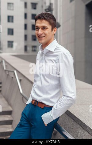 smiling businessman in formal wear standing with hand in pocket near ...
