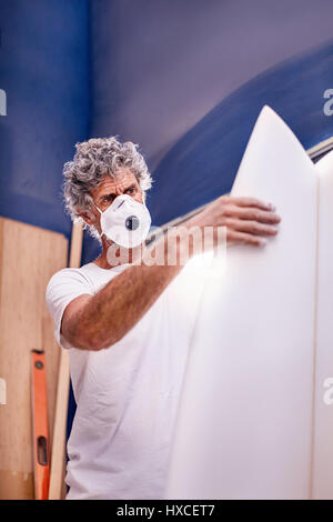 Focused man wearing protective mask sanding surfboard in workshop Stock ...