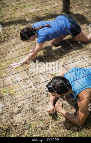 Fit man and woman crawling under the net during obstacle course in boot ...