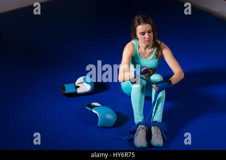 Young female boxer preparing bandages for fight near lying boxing ...