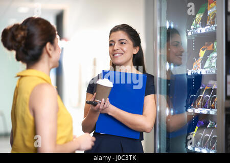 Colleagues using vending machine chatting Stock Photo - Alamy