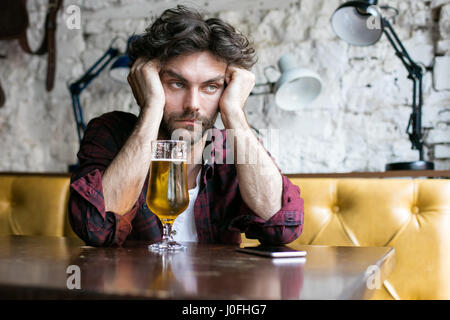 sad and depressed guy having a beer in a pub, sitting alone at a table ...