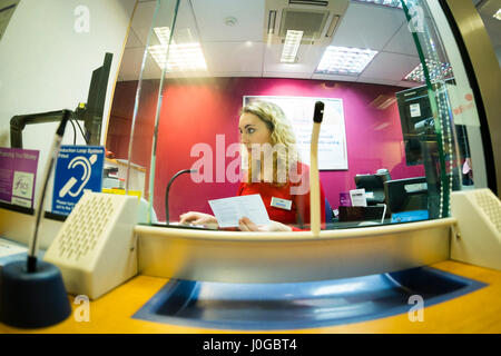 a woman bank teller working behind the counter at a branch of HSBC high ...