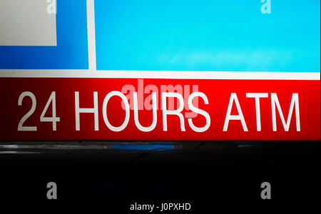 24 hour ATM sign on the roof of a white rendered building set against a ...