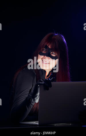 Masked female burglar in black gloves looks over a fence. Crime concept ...