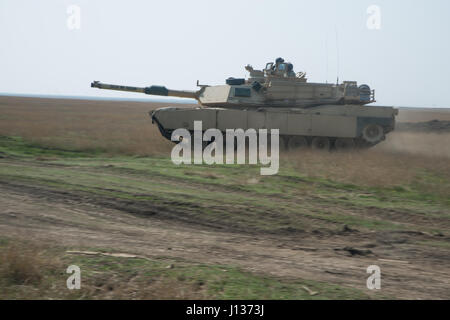 A M1A2 Abrams tank drives by contractors working with 7th Army Training ...
